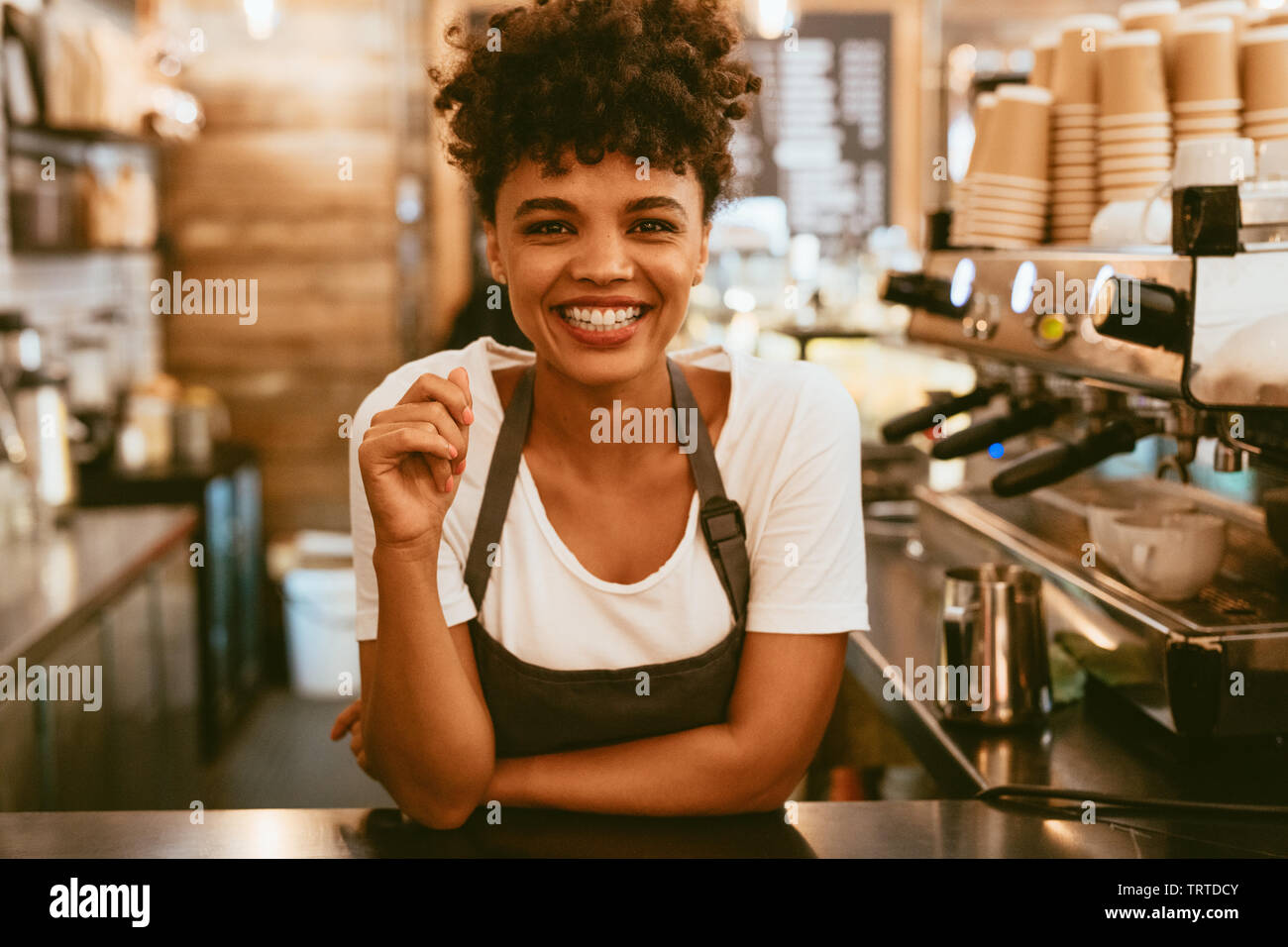 Smiling young woman in apron standing at coffee shop counter. Confident ...