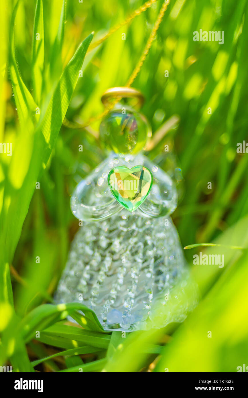 Angel with a green heart in hands stands among the bright green grass ...