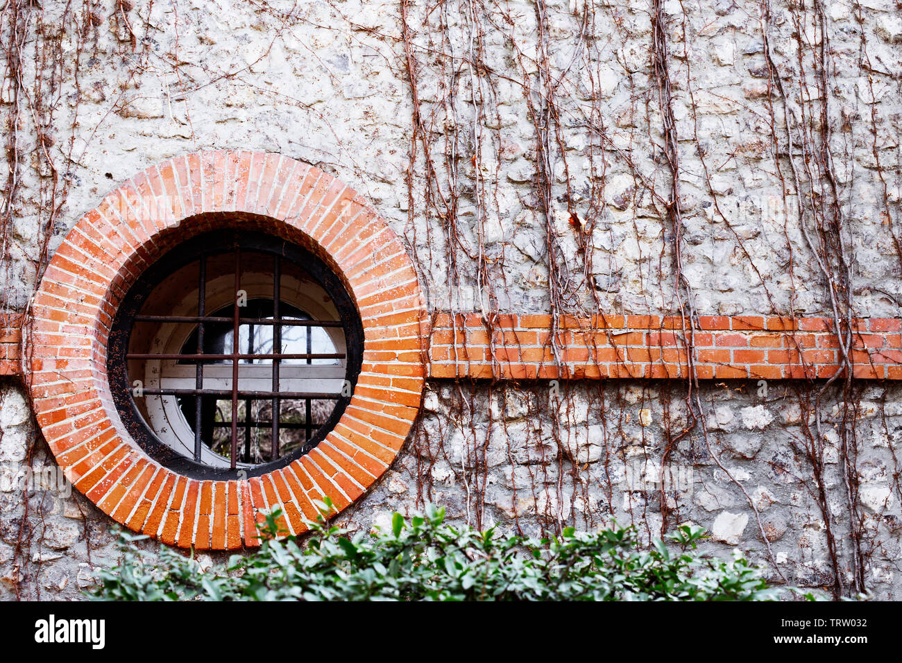 round window with bricks frame on stone facade covered by green leaves ...
