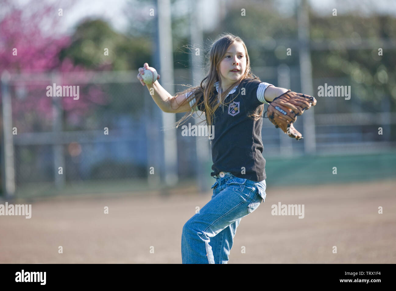 Girl wearing a baseball mitt and winding up to throw a baseball ...