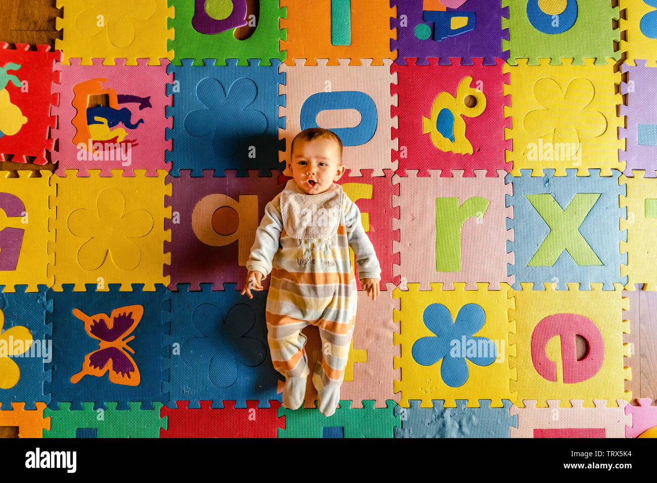 Adorable smiling baby seen from above in pajamas, lying on his back in ...
