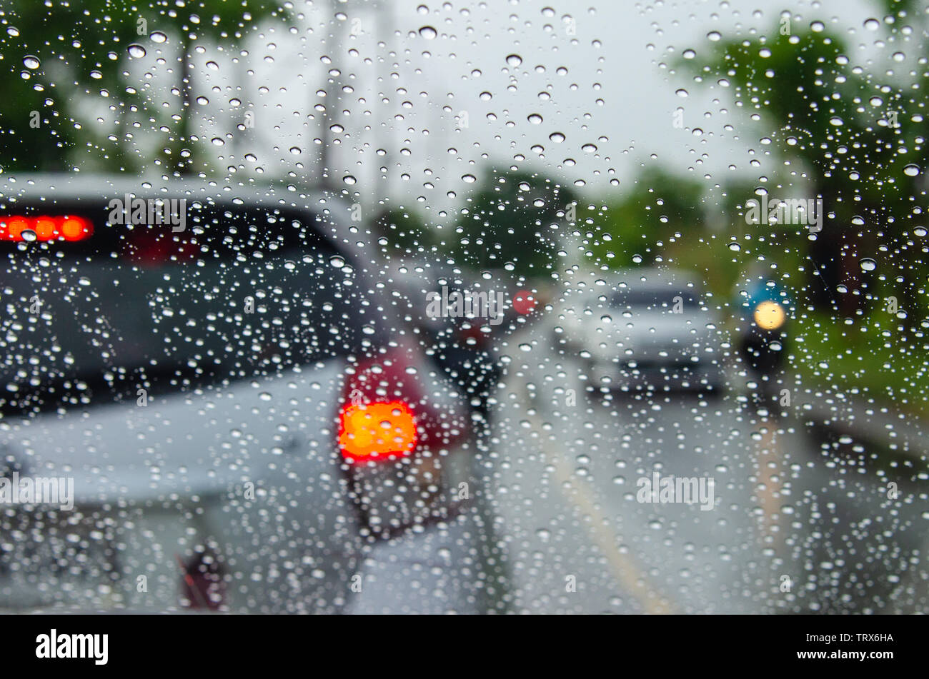 Blurred car images with drops of water at the window, rain on the road ...