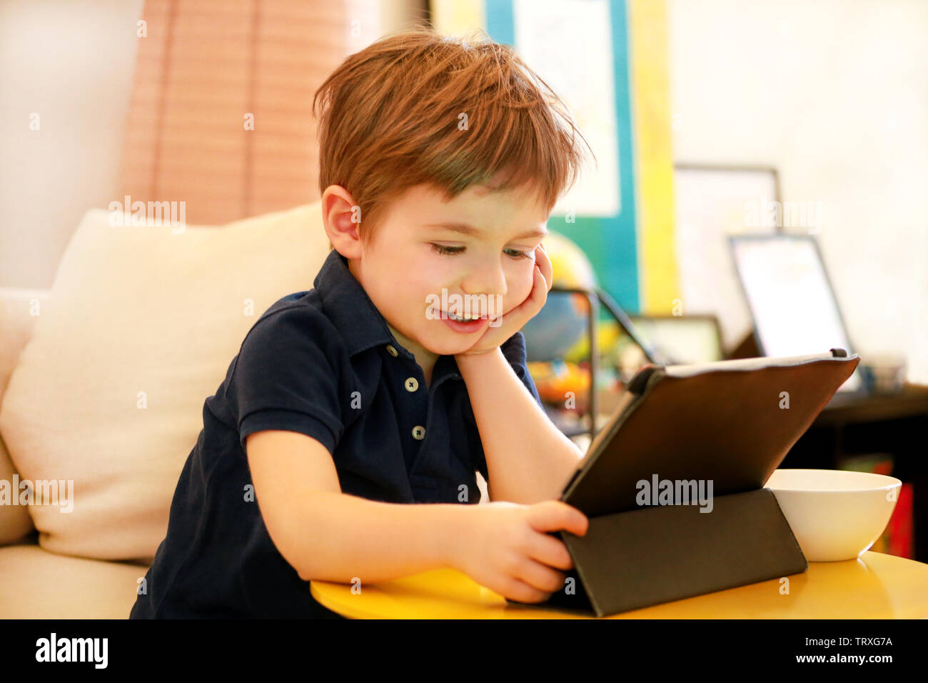 Child using tablet pc on bed at home. Cute boy on sofa is watching ...
