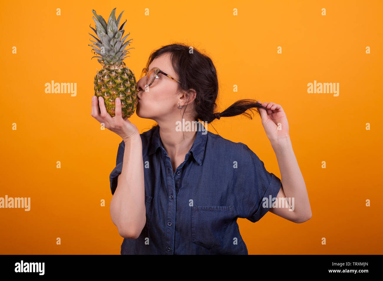 Side view of girl kissing a delicious pineapple in studio over yellow background. Girl kissing ...
