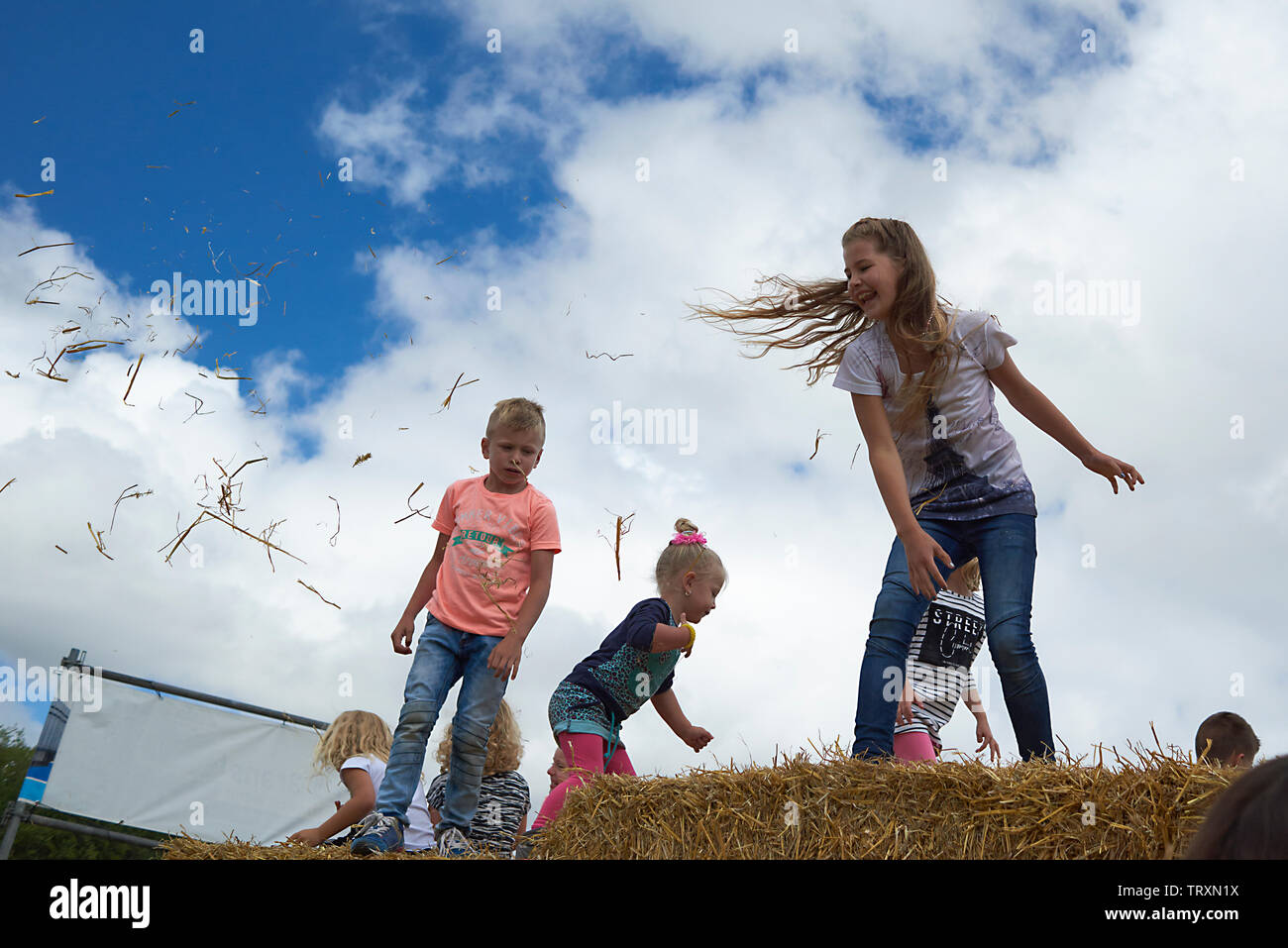 Kids playing on top of a haystack and throwing around the hay in summer ...