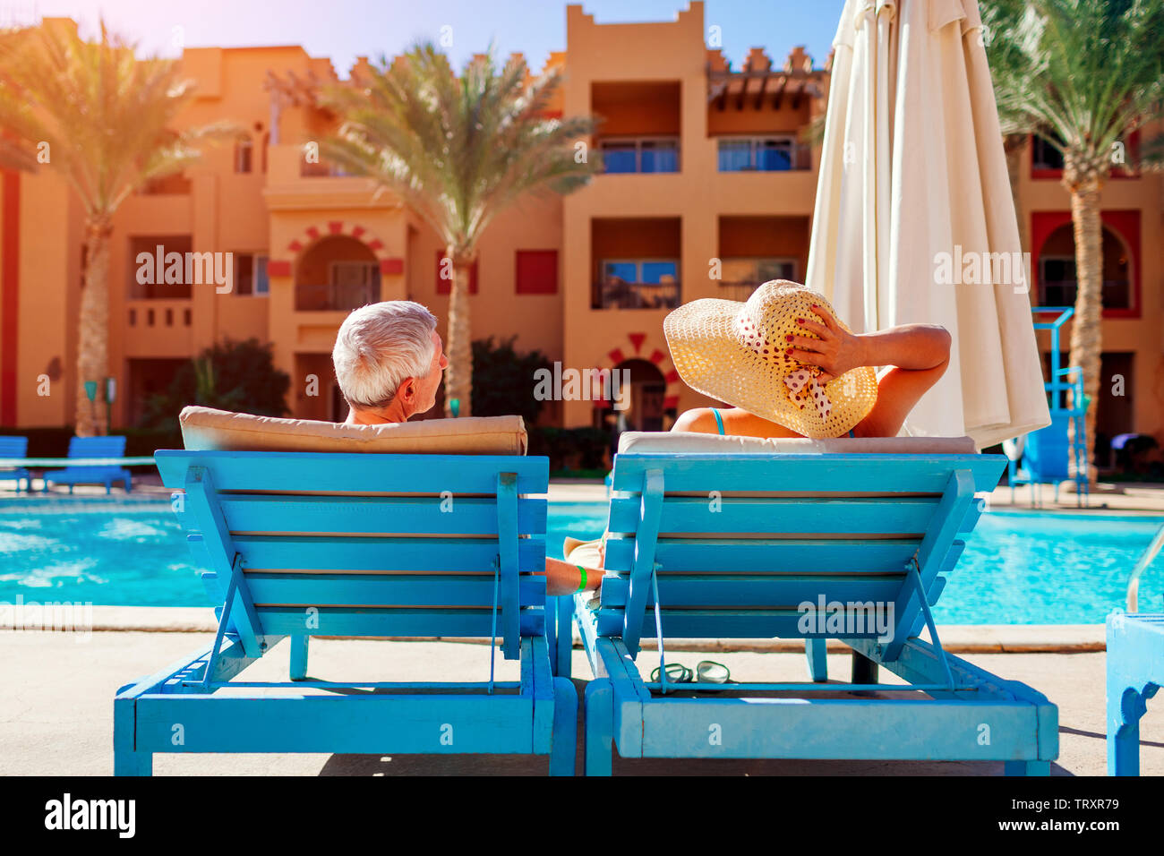 Senior couple relaxing by swimming pool lying on chaise-longues. People ...