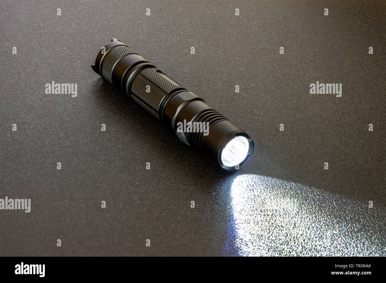 Metallic black LED flashlight on a black background. Light beam on ...