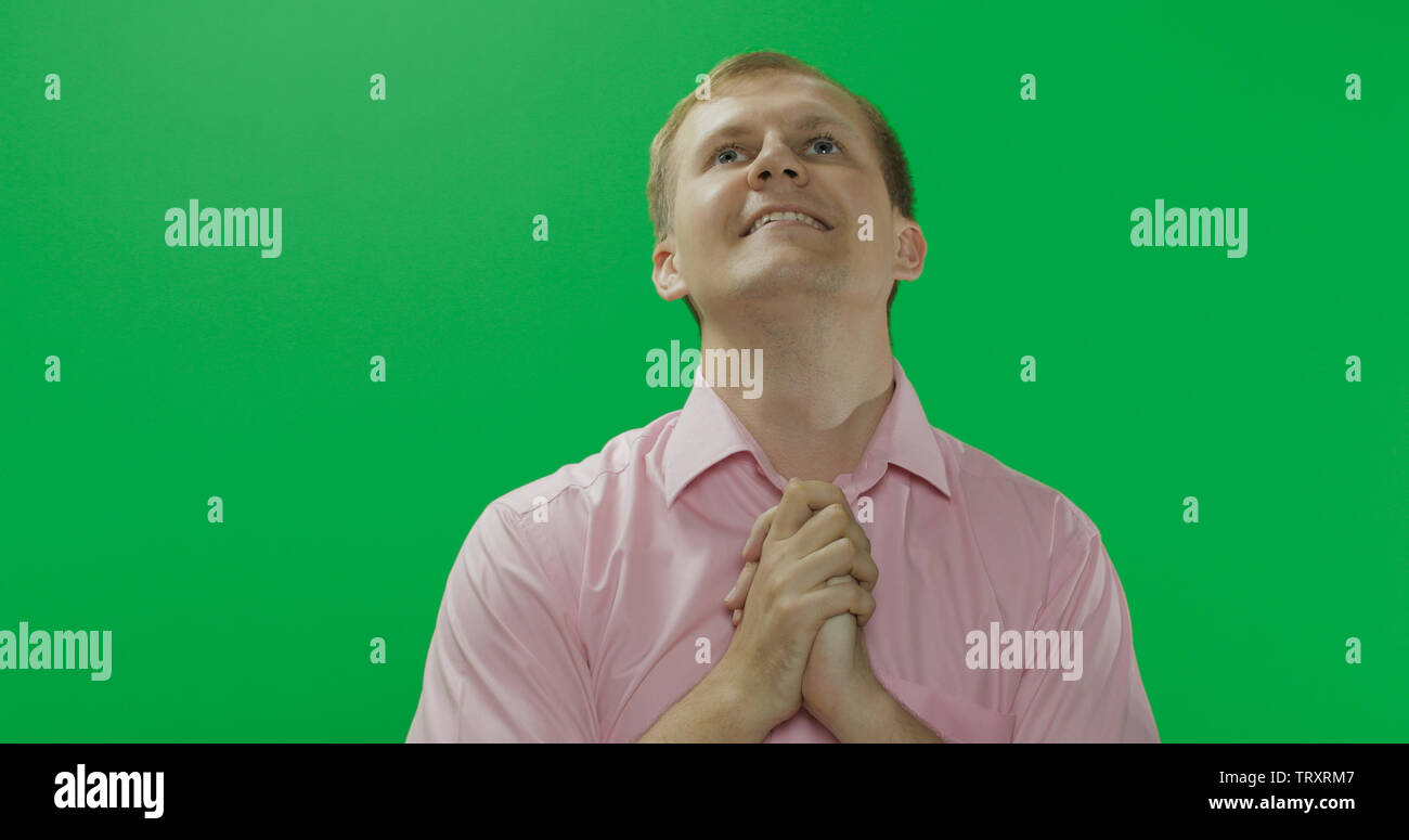Handsome young man in pink shirt praying over a green screen background ...