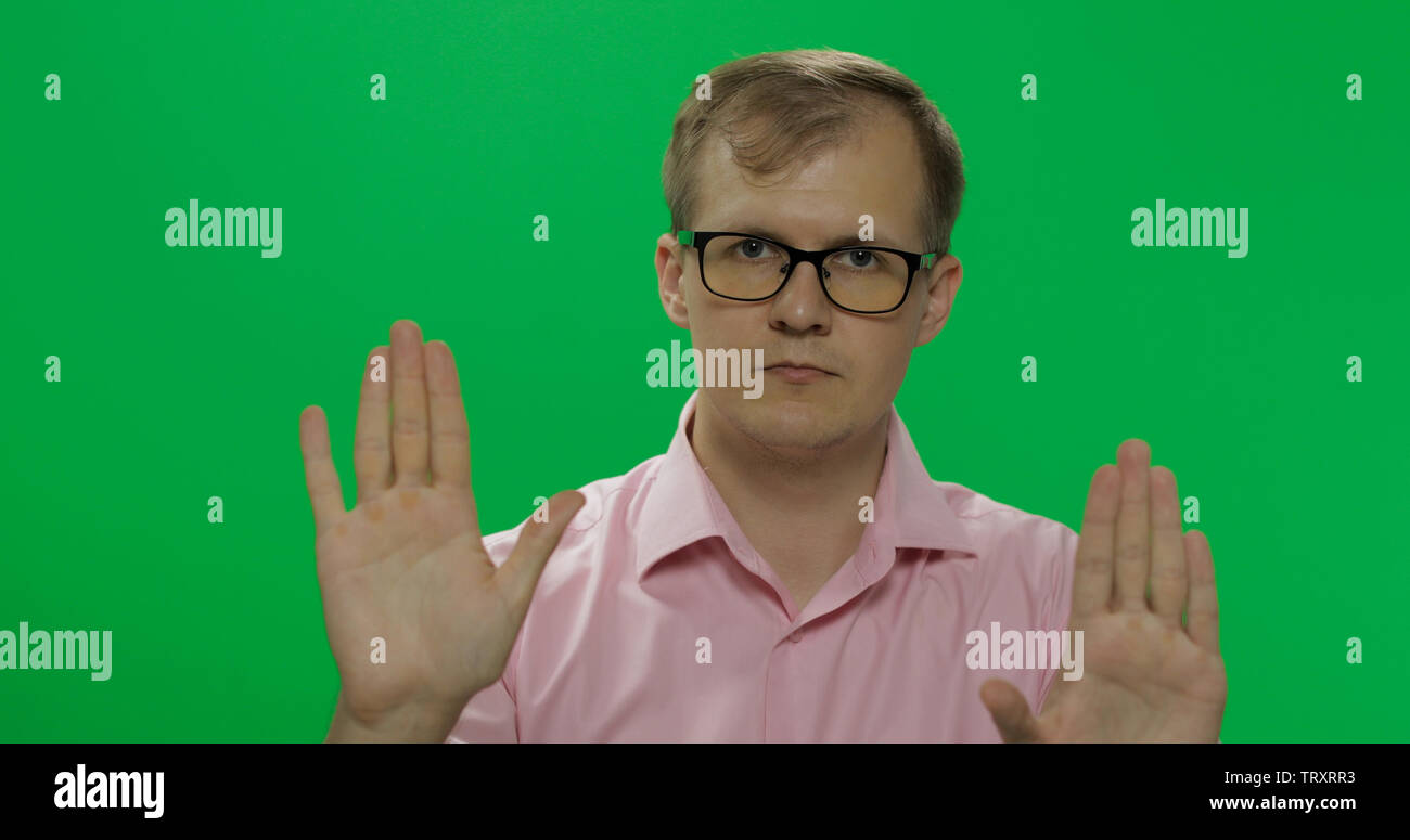 Handsome young man in pink shirt saying no and doing stop gesture with ...
