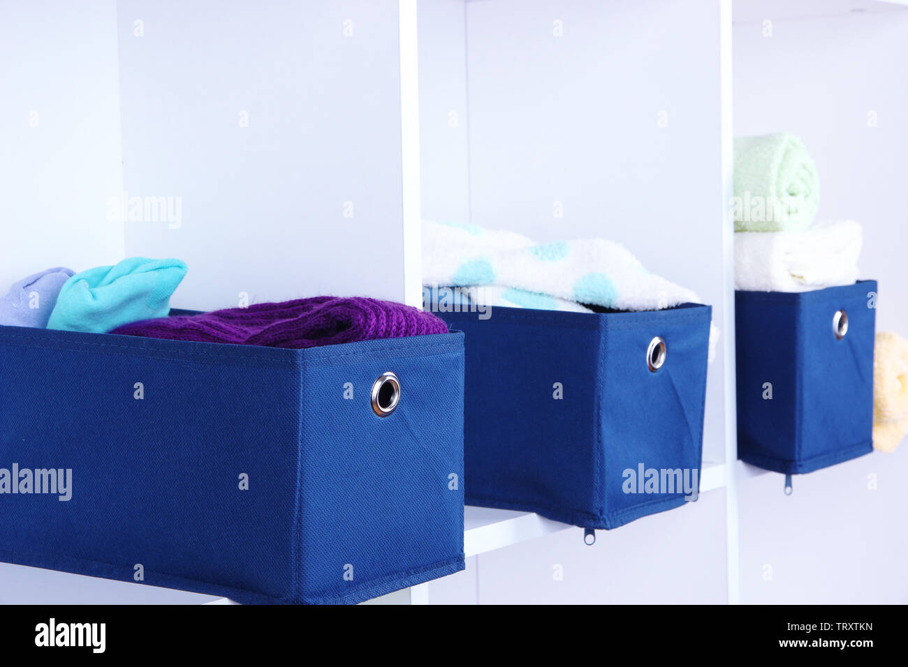 Blue textile boxes with towels and clothes in white shelves Stock Photo ...