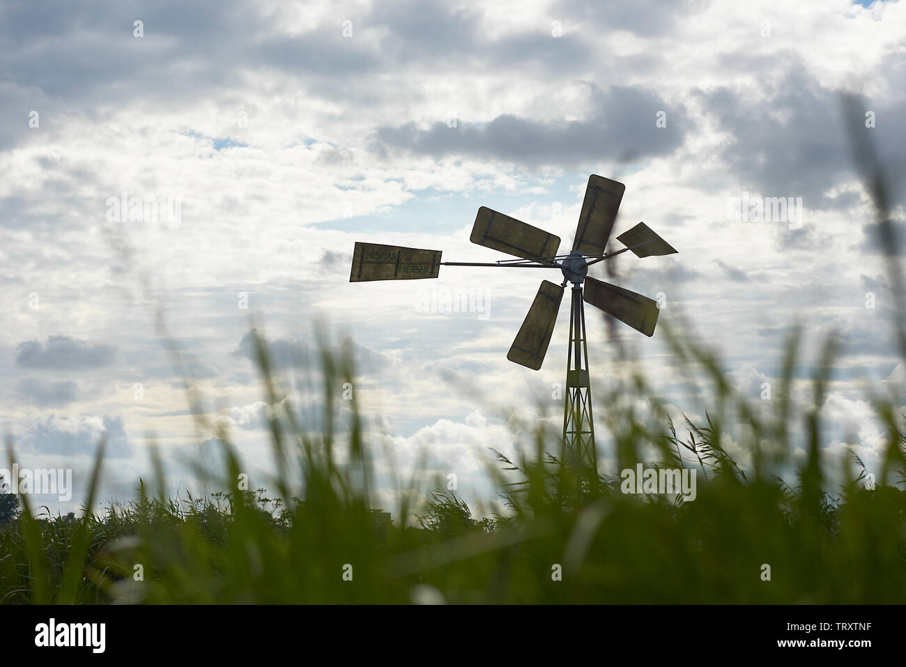 A small metal windmill on farmland in a field in sunshine with wind and ...