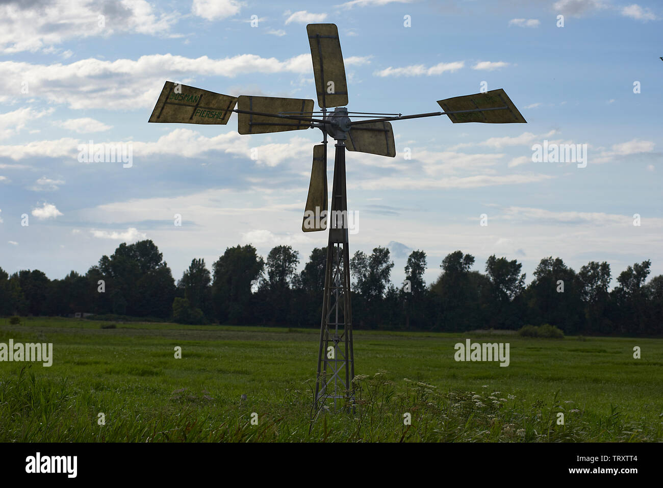 A small metal windmill on farmland in a field in sunshine with wind and ...