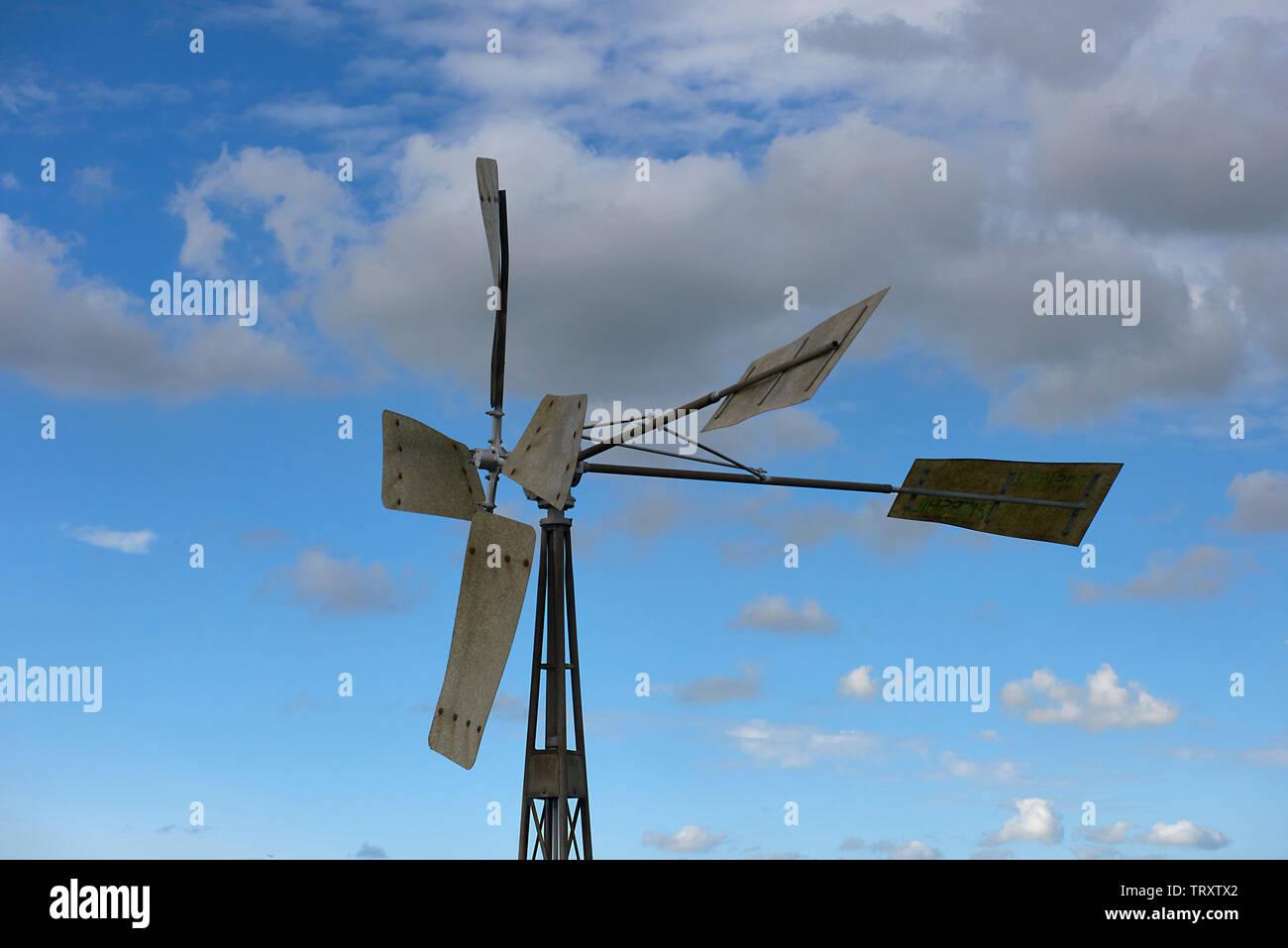 A small metal windmill on farmland in a field in sunshine with wind and ...