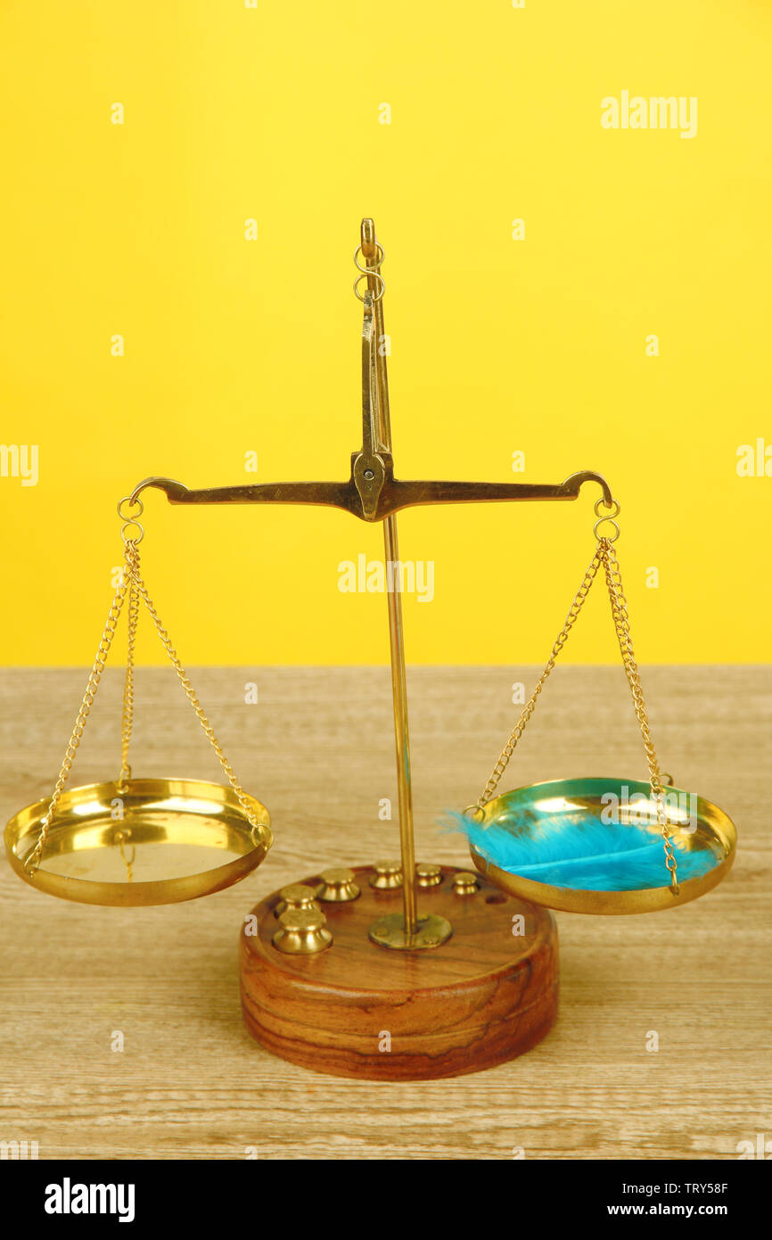 Balance scale with feather on table on yellow background Stock Photo ...