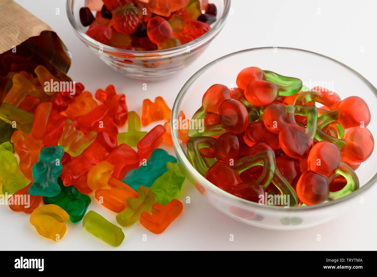 Glass bowls and paper bag of colorful gummy candies on white background ...