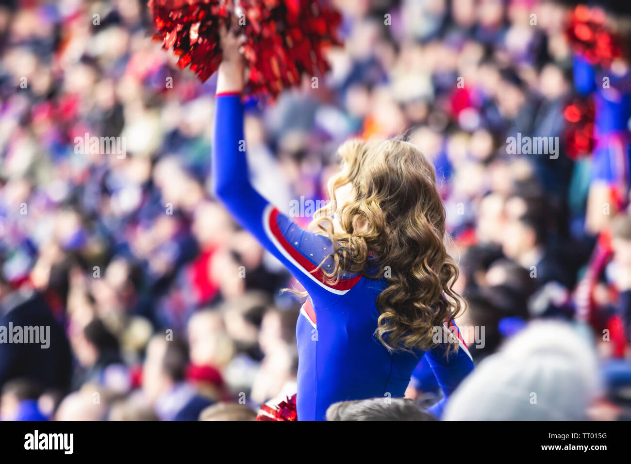 Female cheerleader in red blue uniform with pom-pom with audience in ...