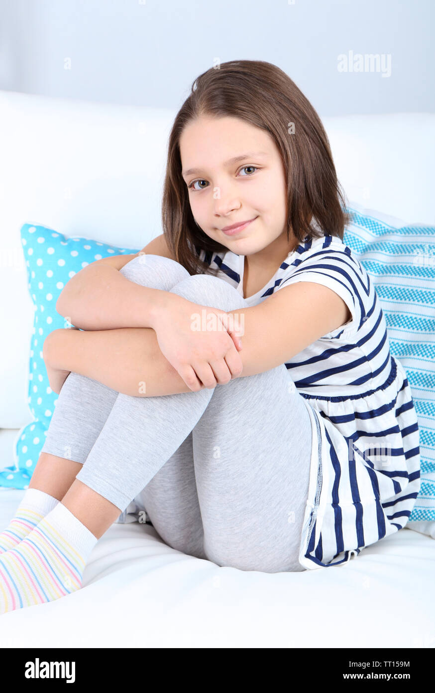 Beautiful little girl sitting on sofa, on home interior background ...
