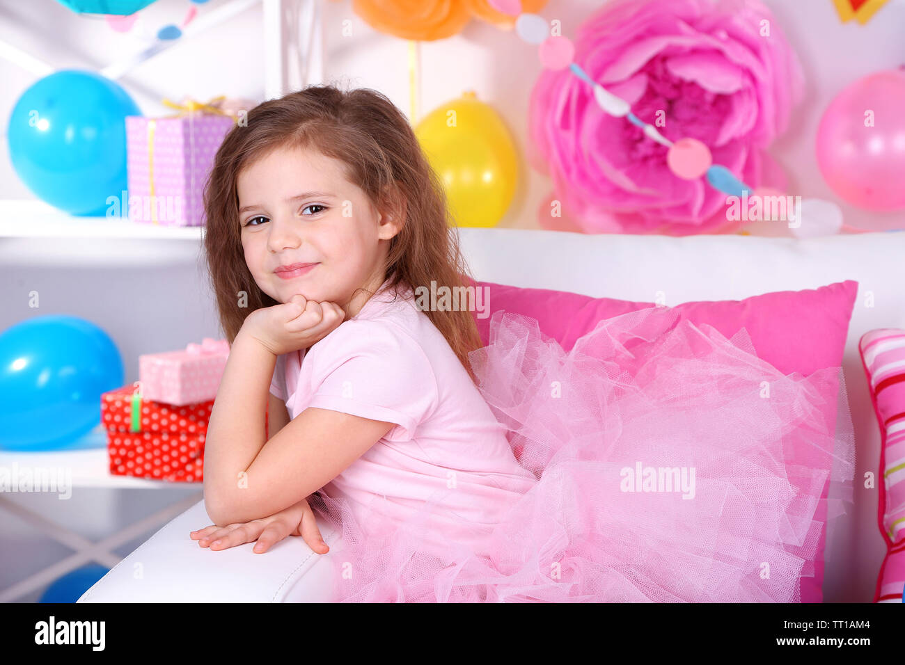 Pretty little girl sitting on sofa on celebratory background Stock ...