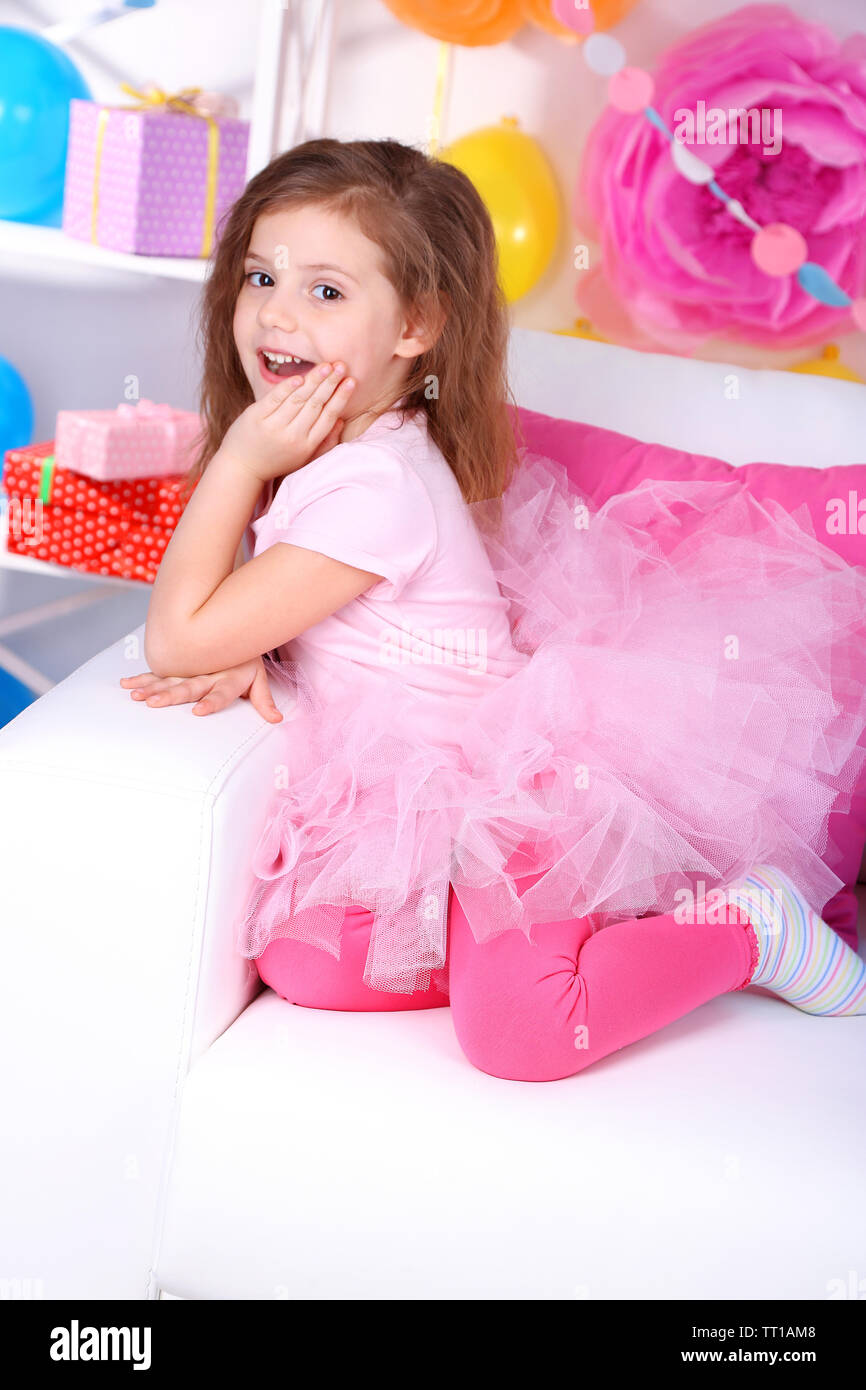 Pretty little girl sitting on sofa on celebratory background Stock ...