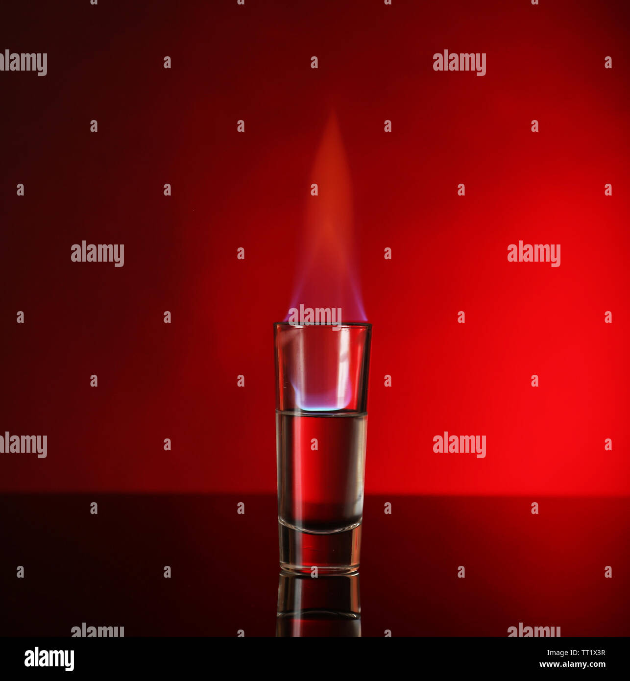 Glass with burning alcohol on red background Stock Photo - Alamy