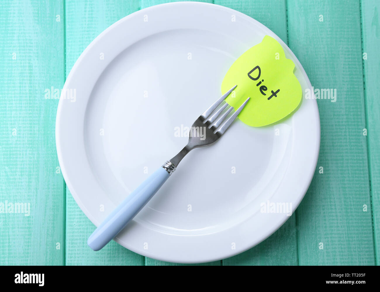 Note paper with message attached to fork, on plate, on color wooden ...