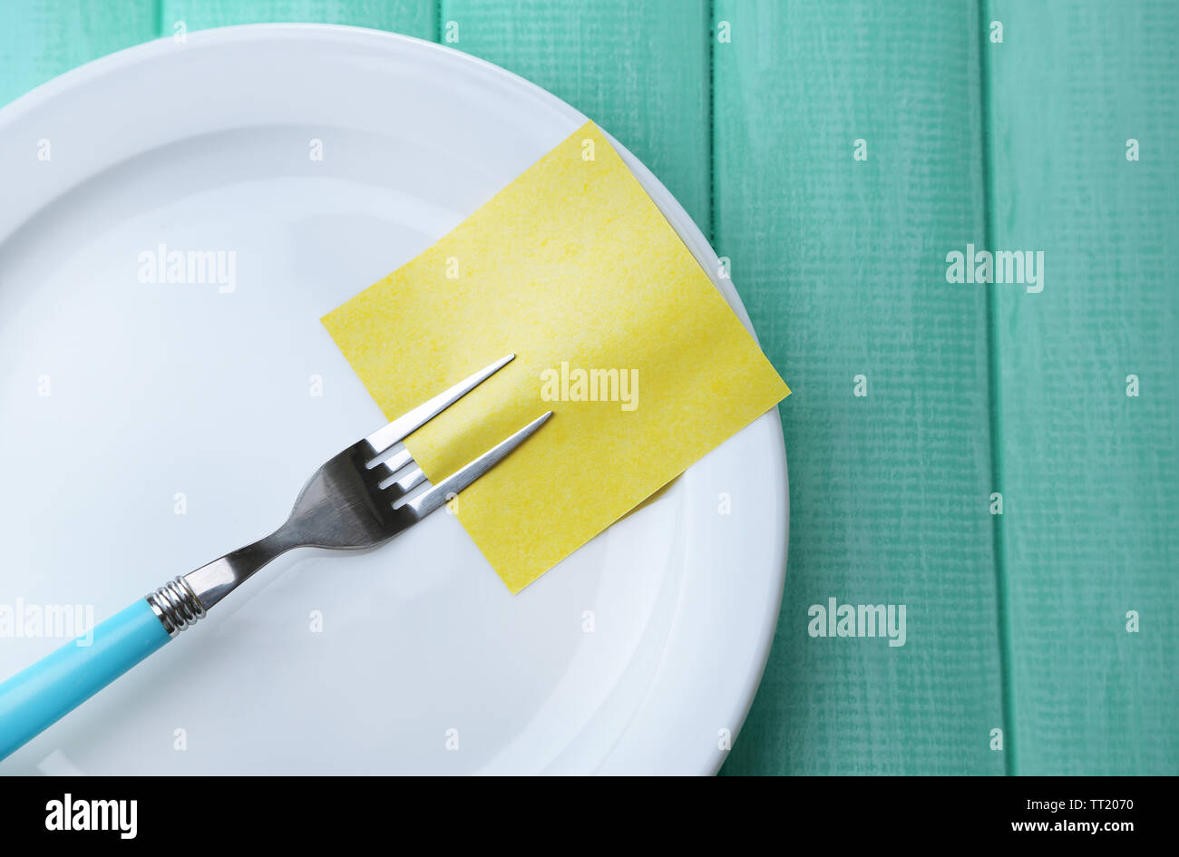 Empty note paper attached to fork, on plate, on color wooden background ...