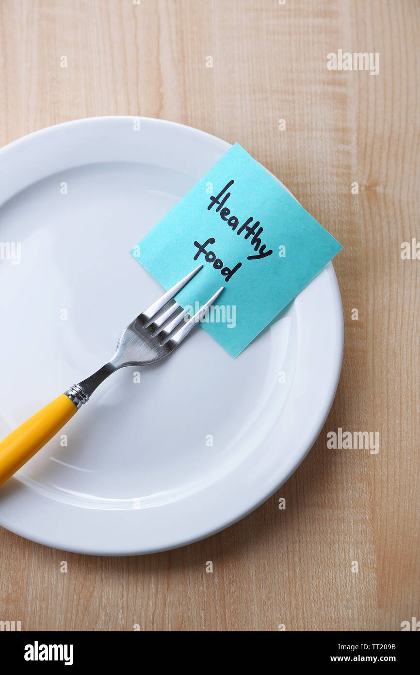Note paper with message attached to fork, on plate, on color wooden ...