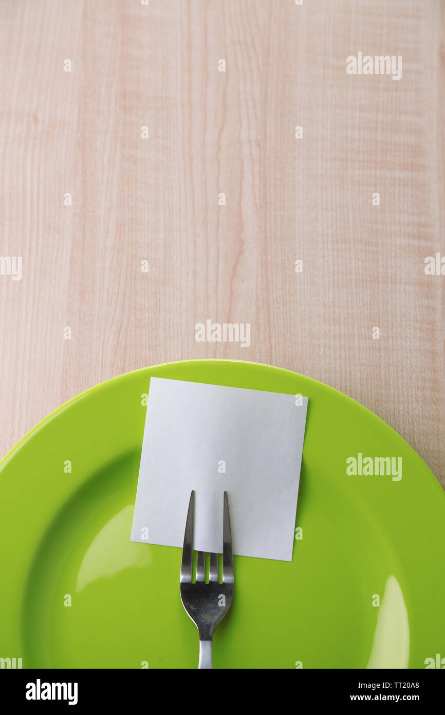 Empty note paper attached to fork, on plate, on color wooden background ...
