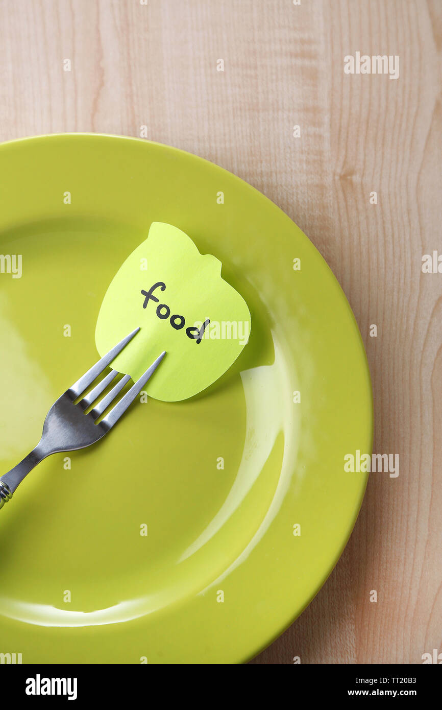 Note paper with message attached to fork, on plate, on color wooden ...