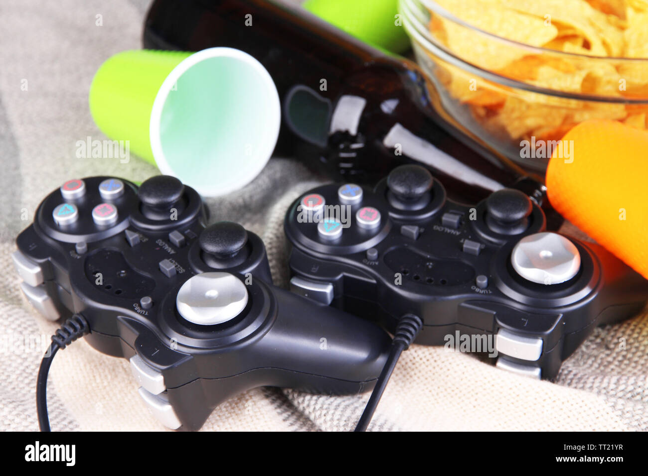 Black game controllers and bowl with snacks on color plaid background ...