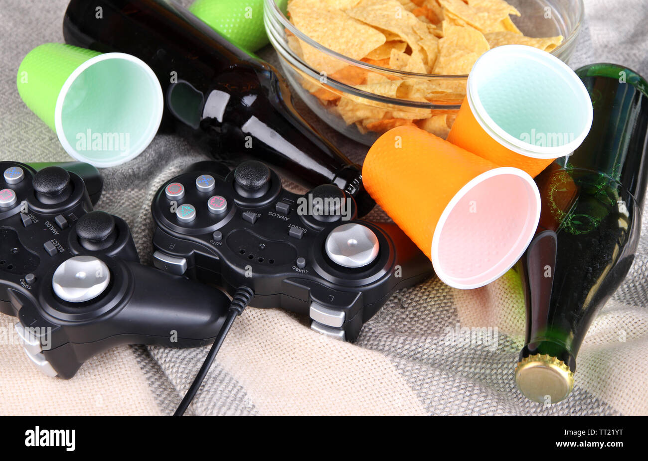 Black game controllers and bowl with snacks on color plaid background ...