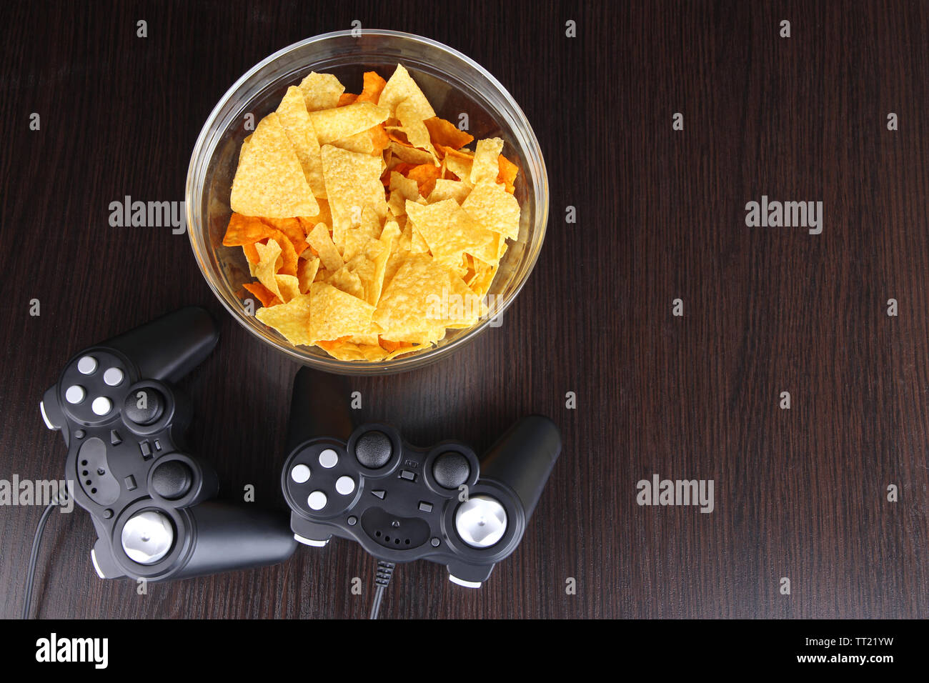 Black game controllers and bowl with snacks on wooden background Stock ...