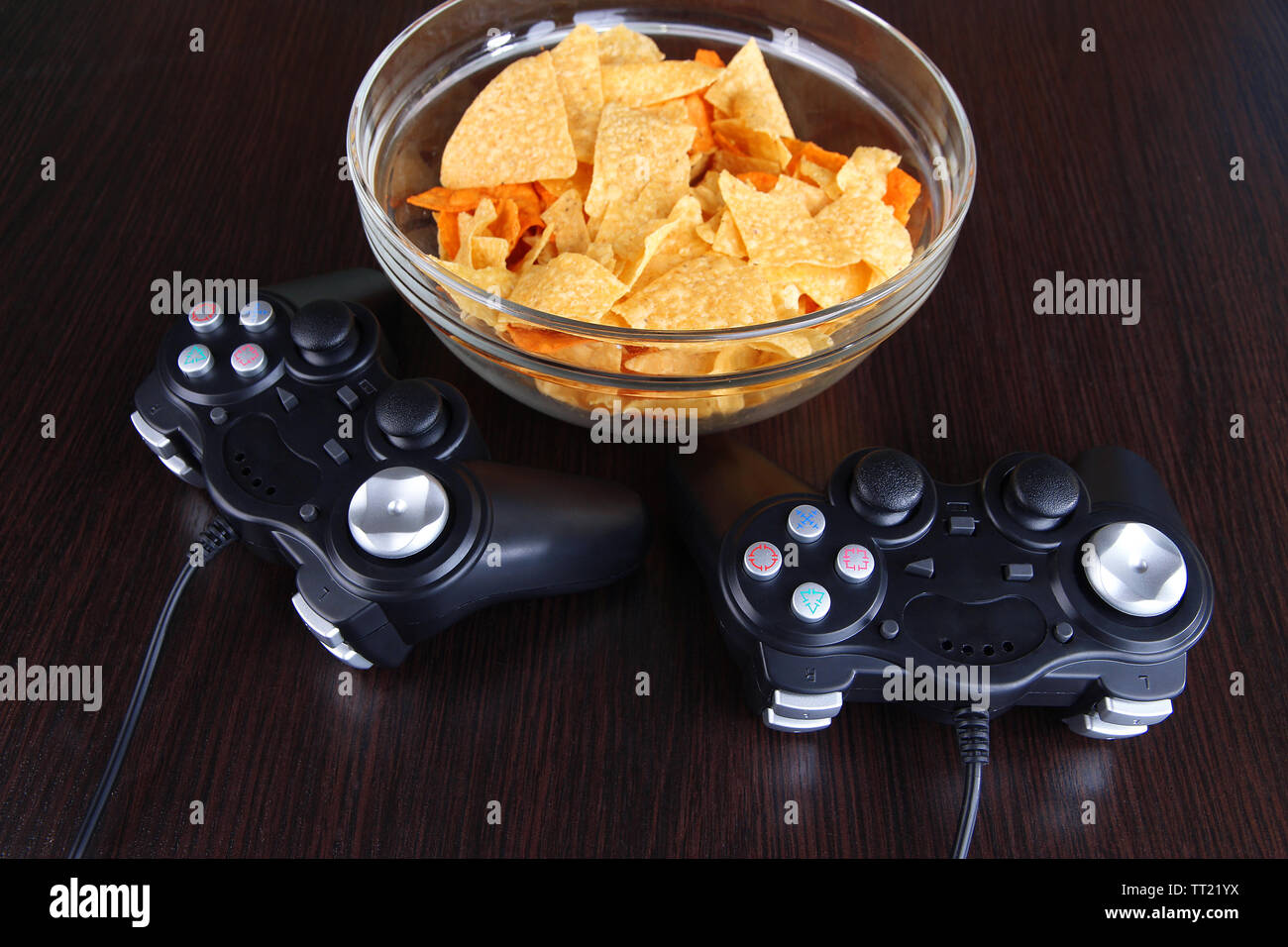 Black game controllers and bowl with snacks on wooden background Stock ...