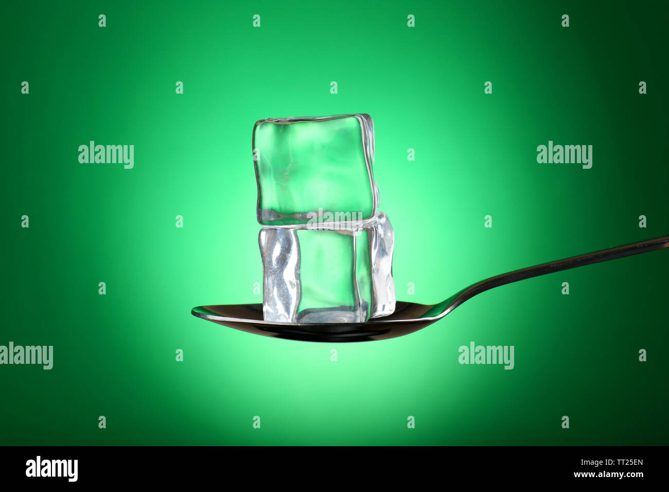 Ice cubes in silver spoon on green background Stock Photo - Alamy