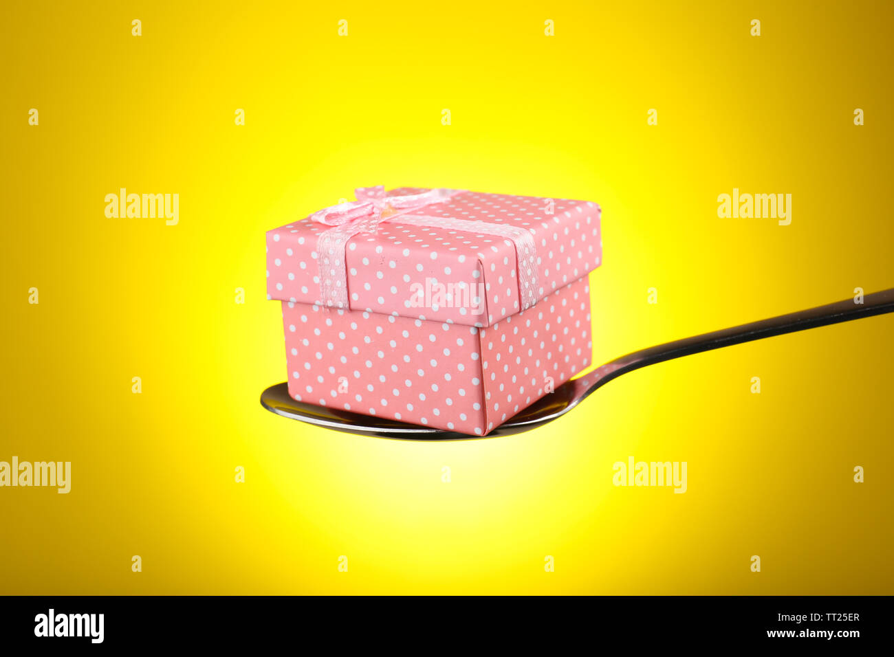 Gift box in silver spoon on yellow background Stock Photo - Alamy