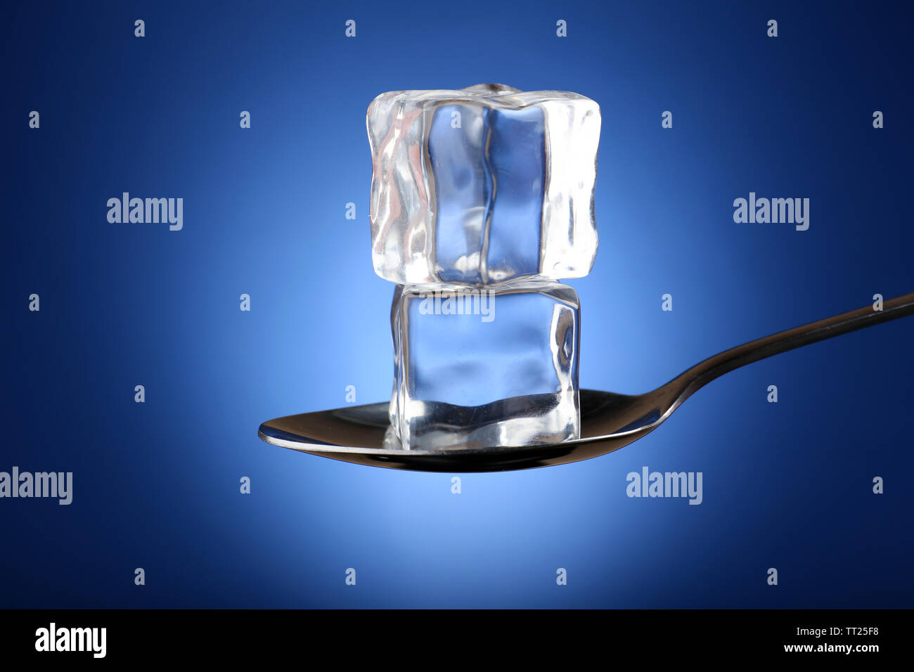 Ice cubes in silver spoon on blue background Stock Photo - Alamy