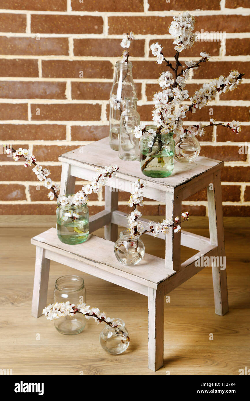 Beautiful apricot blossom in transparent jars on brick wall background ...