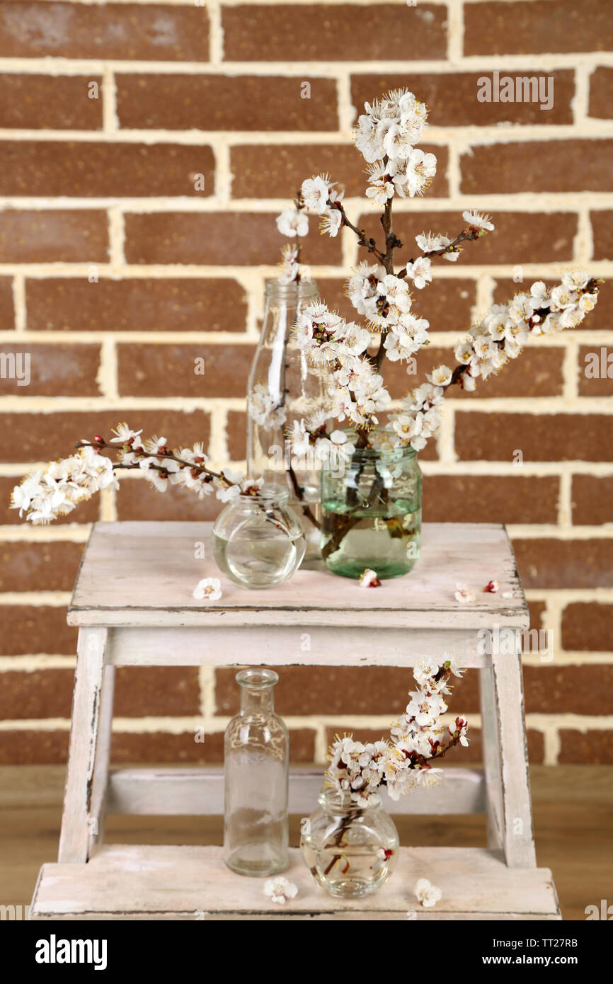 Beautiful apricot blossom in transparent jars on brick wall background ...