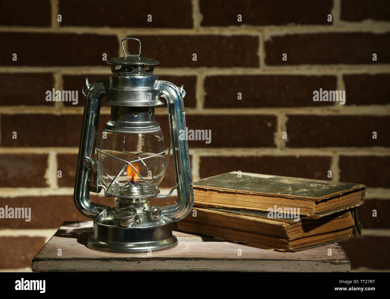 Burning kerosene lamp and books on brick wall background Stock Photo ...