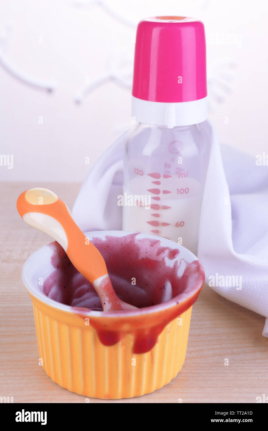 Baby bottle with milk and dirty bowl on table on light background Stock ...