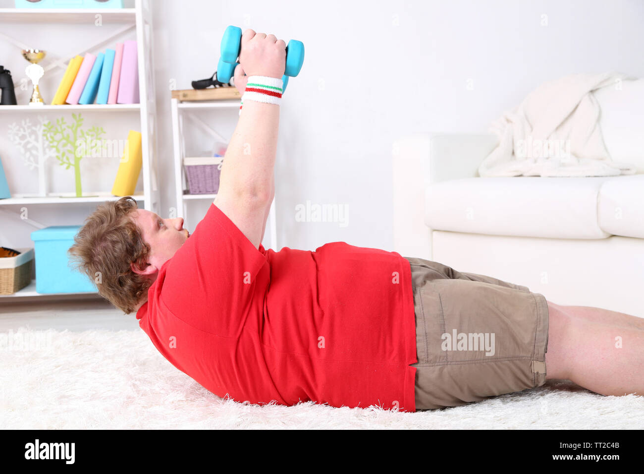 Large fitness man making exercises with dumbbells on floor, at home ...