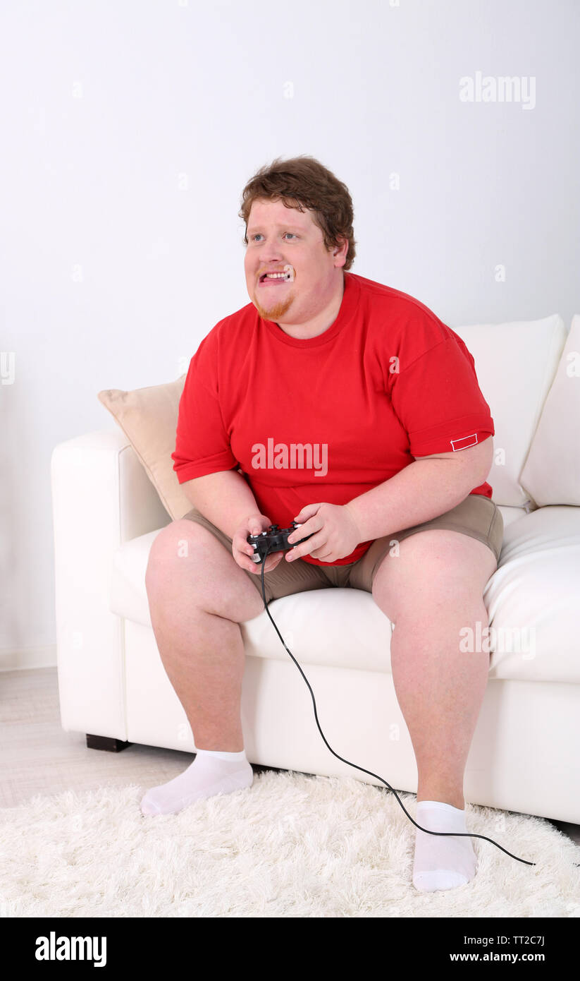 Fat man playing video games on home interior background Stock Photo - Alamy