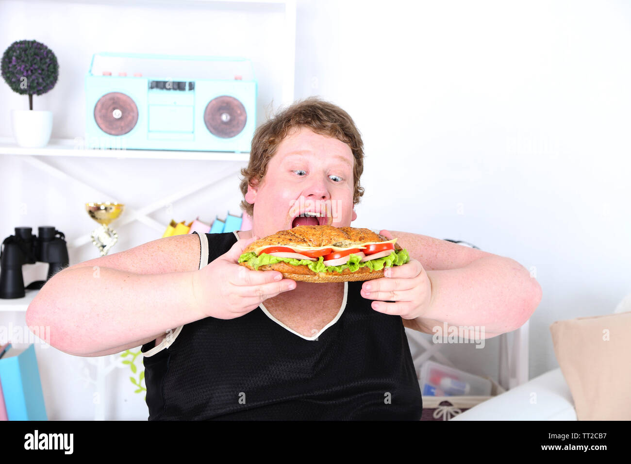 Fat man eating tasty sandwich on home interior background Stock Photo ...