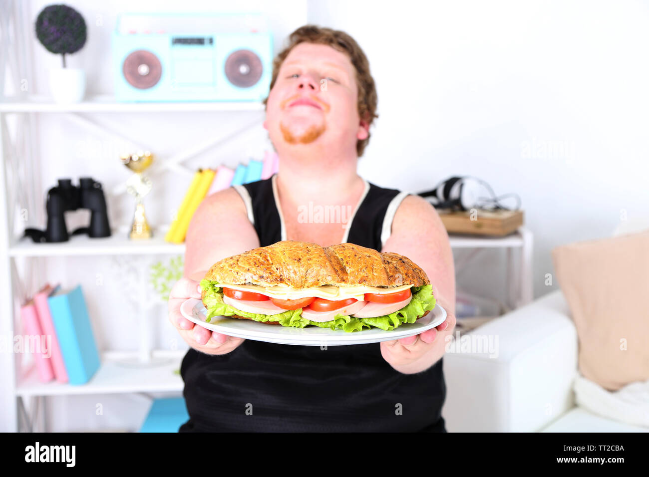 Fat man eating tasty sandwich on home interior background Stock Photo ...