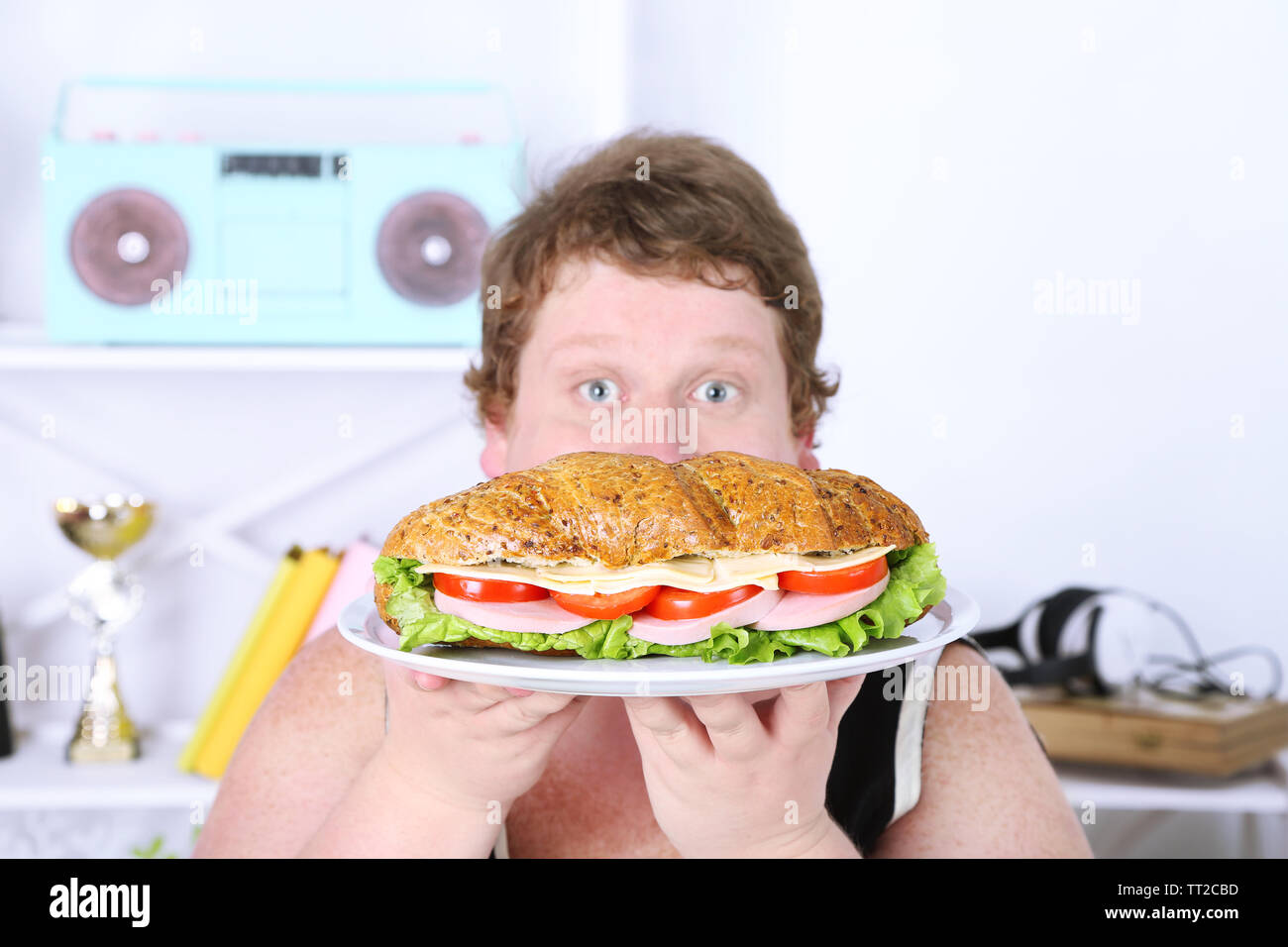 Fat man eating tasty sandwich on home interior background Stock Photo ...