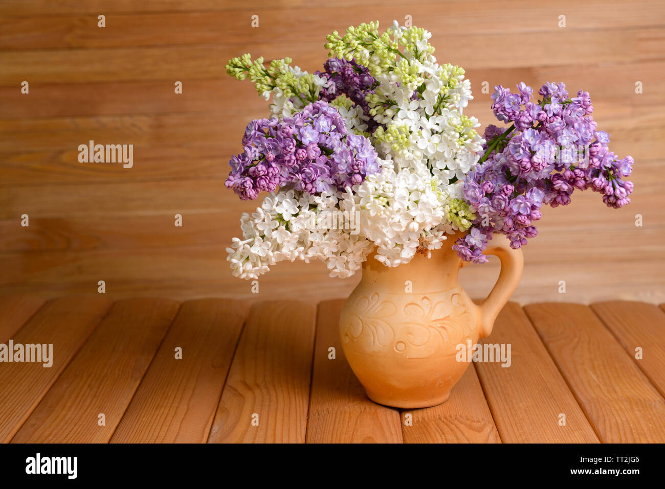 Beautiful lilac flowers in pitcher on table on wooden background Stock ...