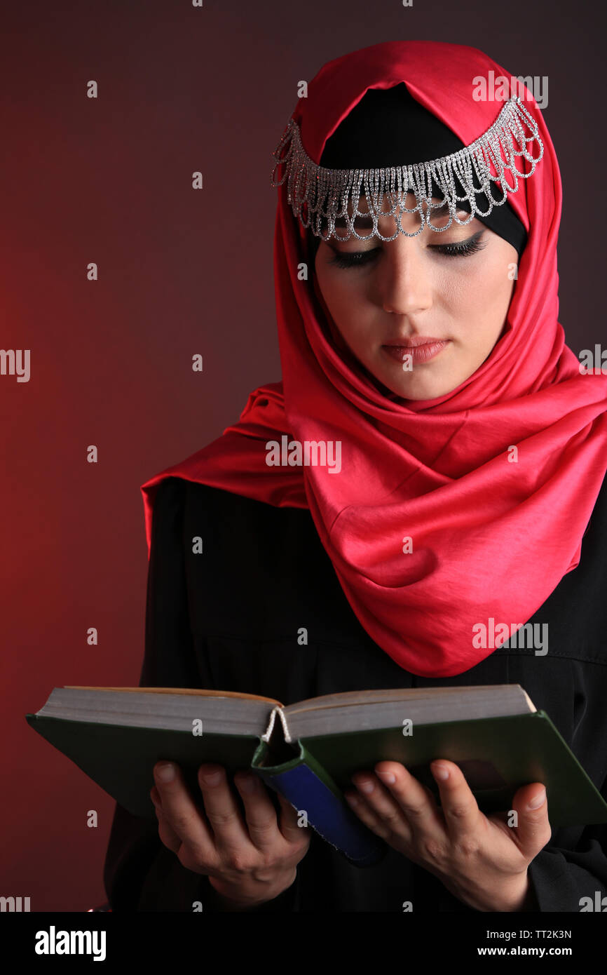 Beautiful muslim arabic woman reading book on dark color background ...