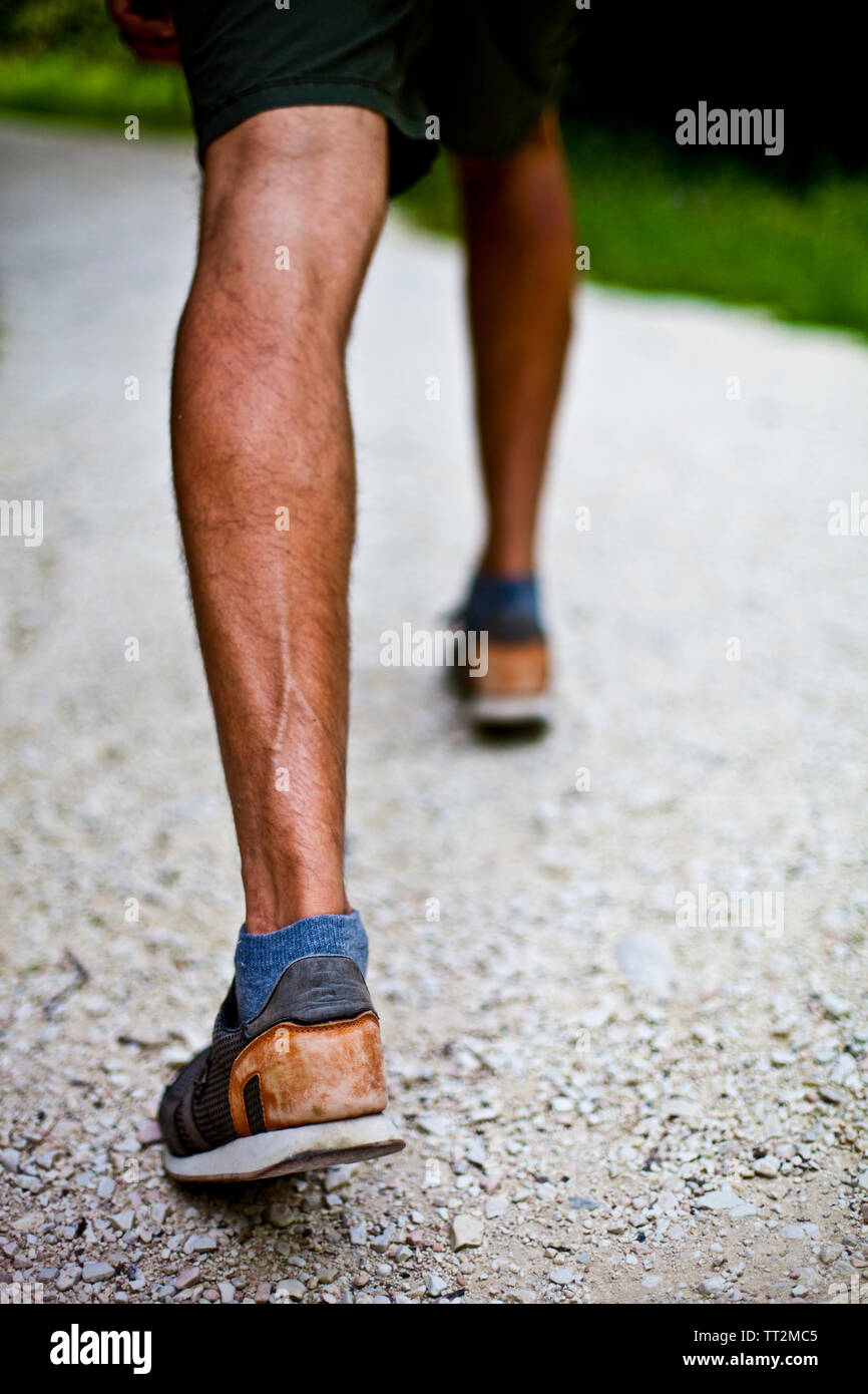 Low angle ground level view with feet of a man on park or forest path ...