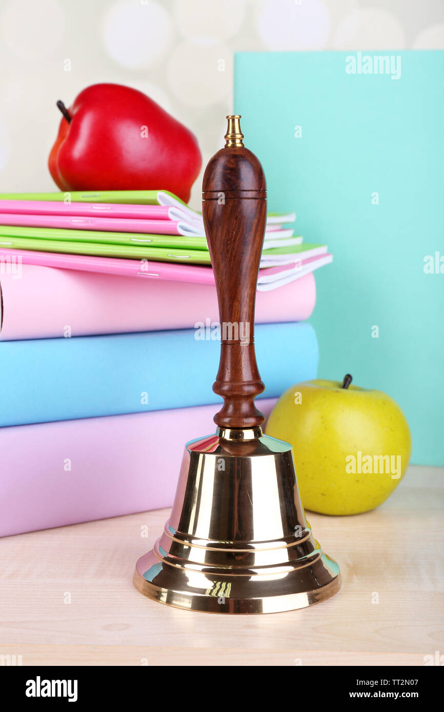 Gold school bell with school supplies on table on bright background ...
