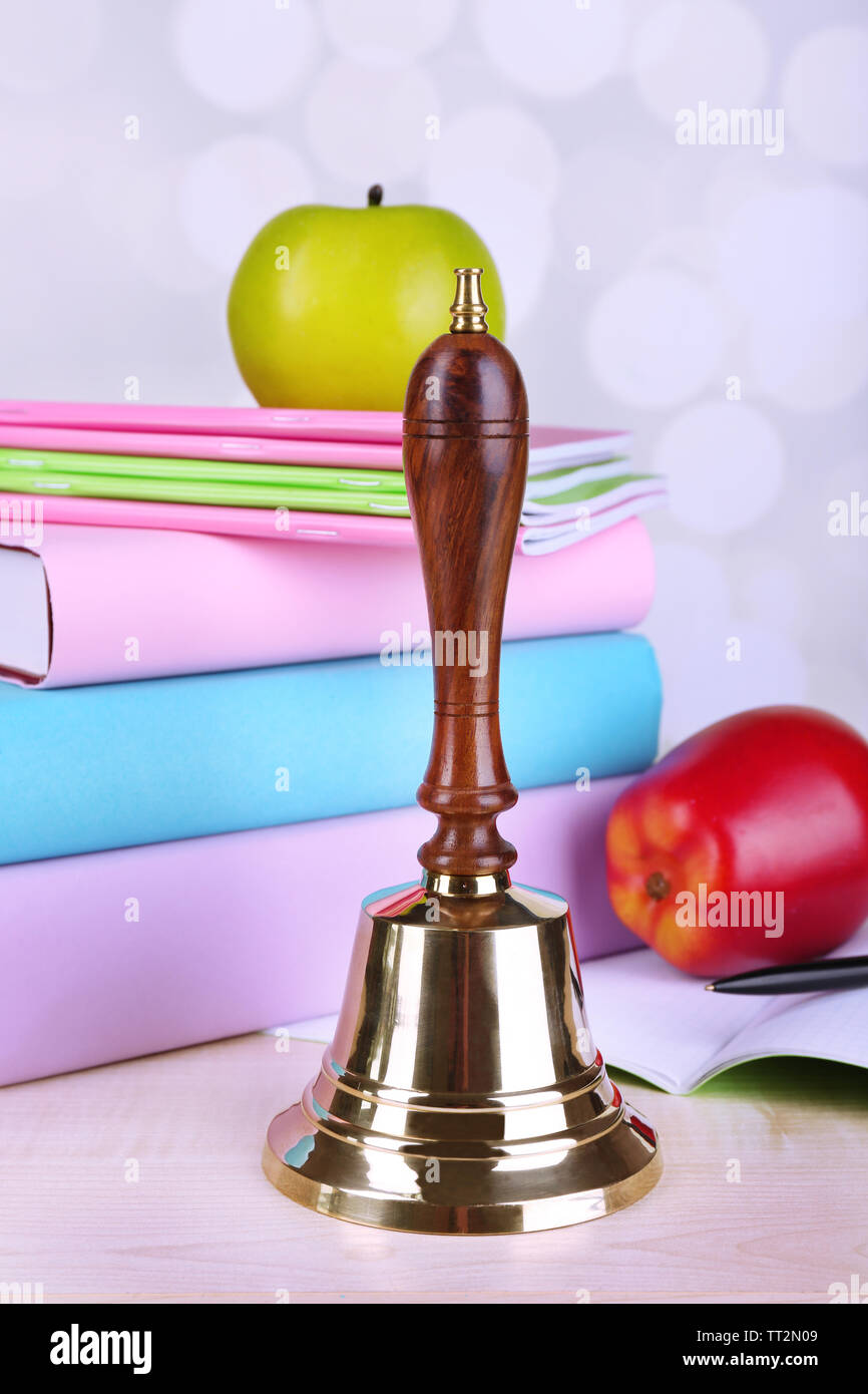 Gold school bell with school supplies on table on bright background ...